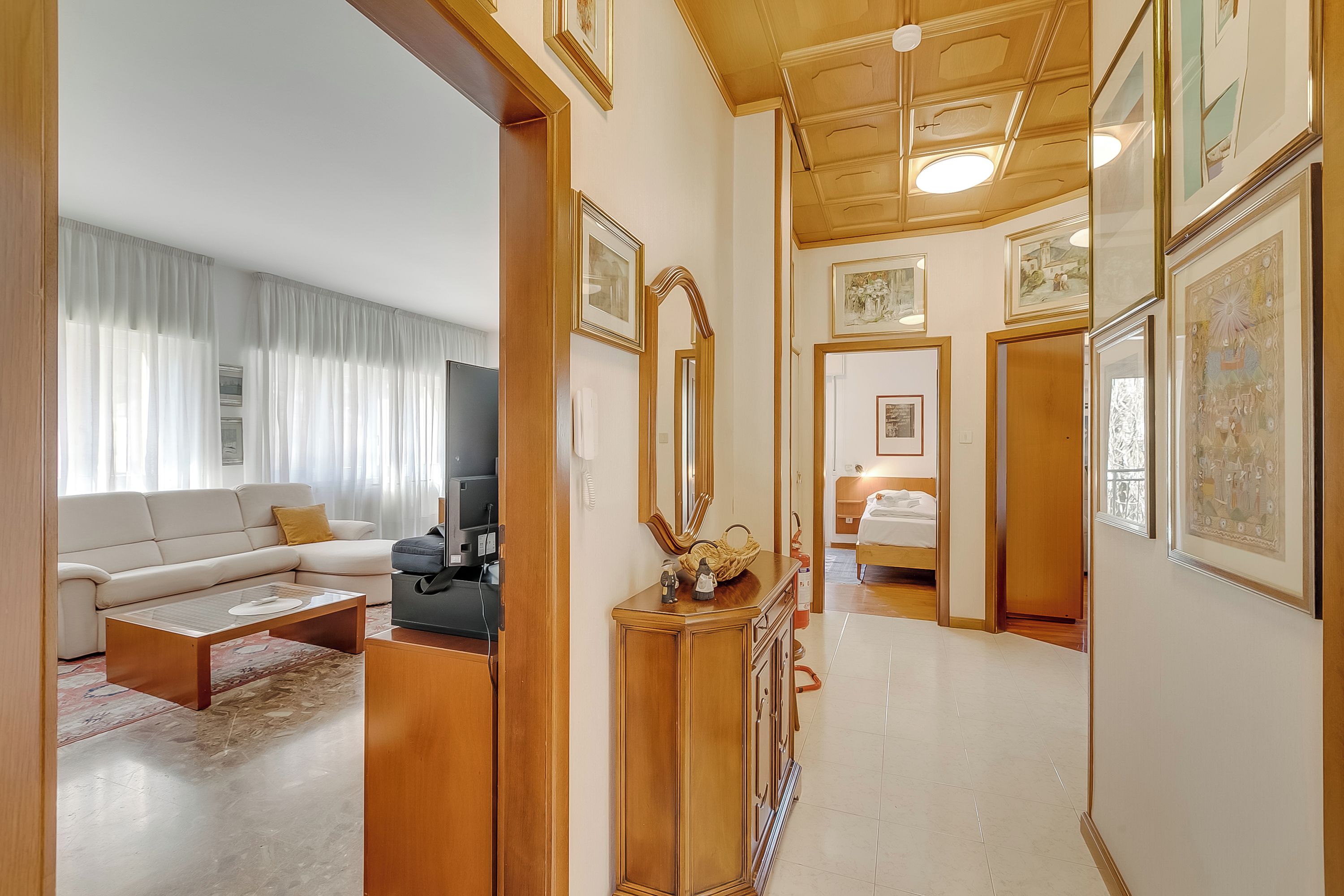 Sala de estar com sofá, mesa de centro e televisão, corredor com quadros, e quarto com cama.