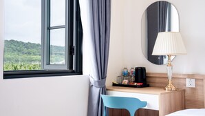 Quarto de hotel com janela, escrivaninha com luminária, uma cadeira e uma cama.