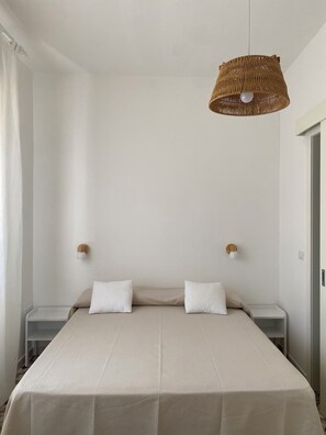 Quarto com cama, duas mesas de cabeceira, luminária pendente e uma porta.