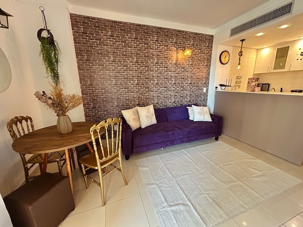 Um espaço de estar moderno com parede de tijolos, sofá roxo, mesa de jantar de madeira e um lustre.
