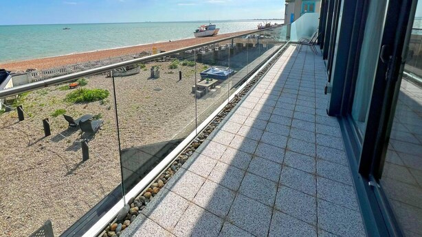 Varanda com vista para a praia e o mar, chão de azulejos e guarda-corpo.