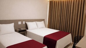 Quarto de hotel com duas camas de solteiro, mesa de cabeceira, escrivaninha e uma cadeira.