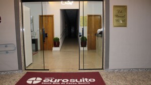Entrada de hotel com porta de vidro, balcão de recepção e placa indicando o nome 'Euro Suite'.