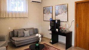 Uma sala de estar com um sofá cinza, uma mesa de centro com um vaso, e duas pinturas abstratas na parede.