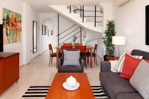 Uma sala de estar moderna com sofá, mesa de centro, área de jantar com cadeiras e mesa, escada e uma grande pintura abstrata.
