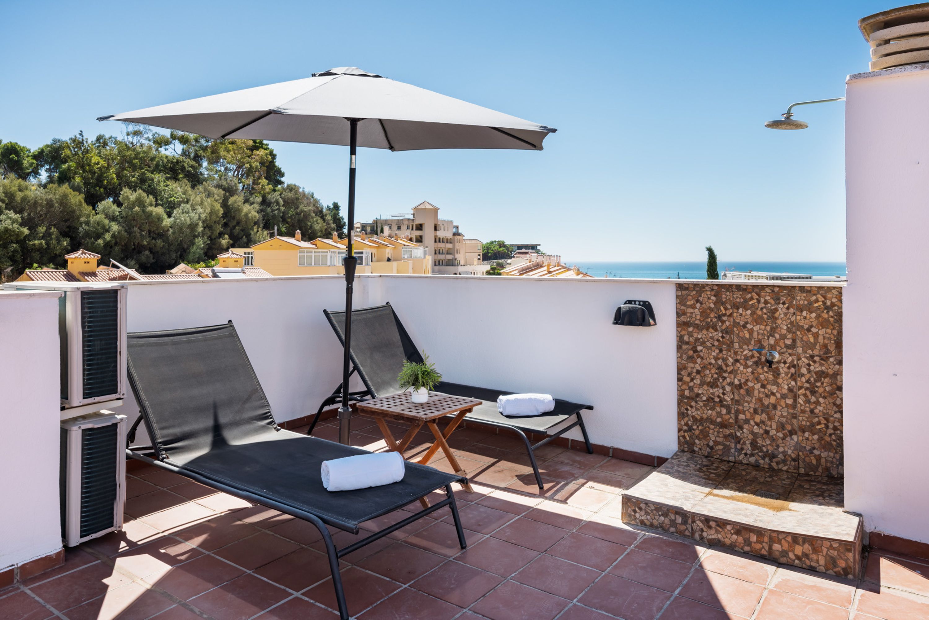 Terraço no telhado com duas cadeiras de descanso, uma mesa e um guarda-sol.