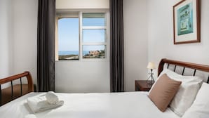 Quarto de hotel com cama, mesa de cabeceira, luminária, janela com cortinas e um quadro na parede.