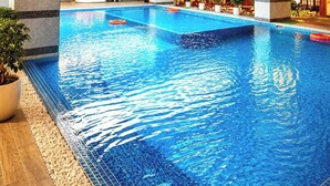 Piscina interna com vigas de madeira, piso ladrilhado e área de estar com mesa e cadeiras.