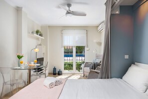 Quarto de hotel com cama, escrivaninha, cadeira, ventilador de teto e varanda com vista.