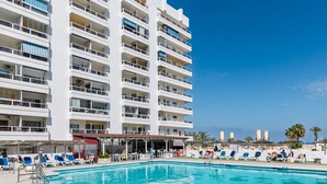 Um hotel com piscina, várias varandas e uma área coberta com espreguiçadeiras.