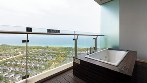 Varanda com vista para uma área residencial e o mar, banheira e guarda-corpo de vidro.