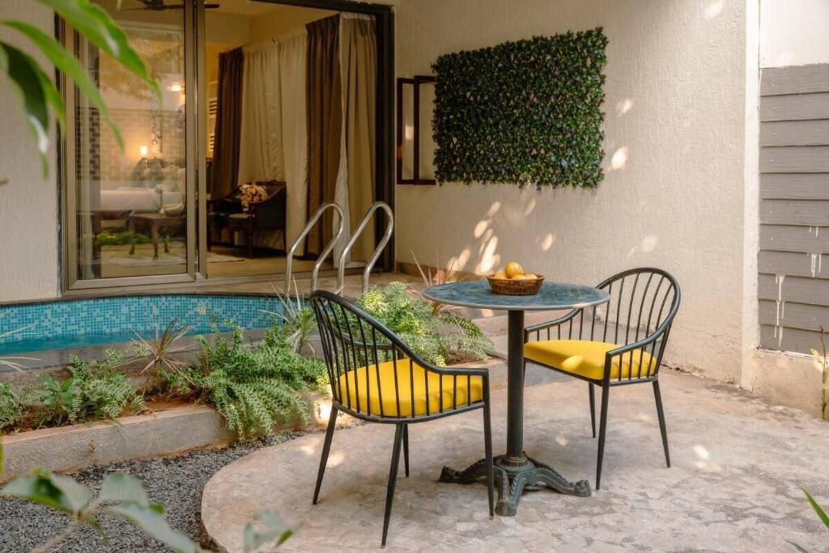 Um pátio com duas cadeiras, uma mesa, uma piscina pequena e uma parede verde.