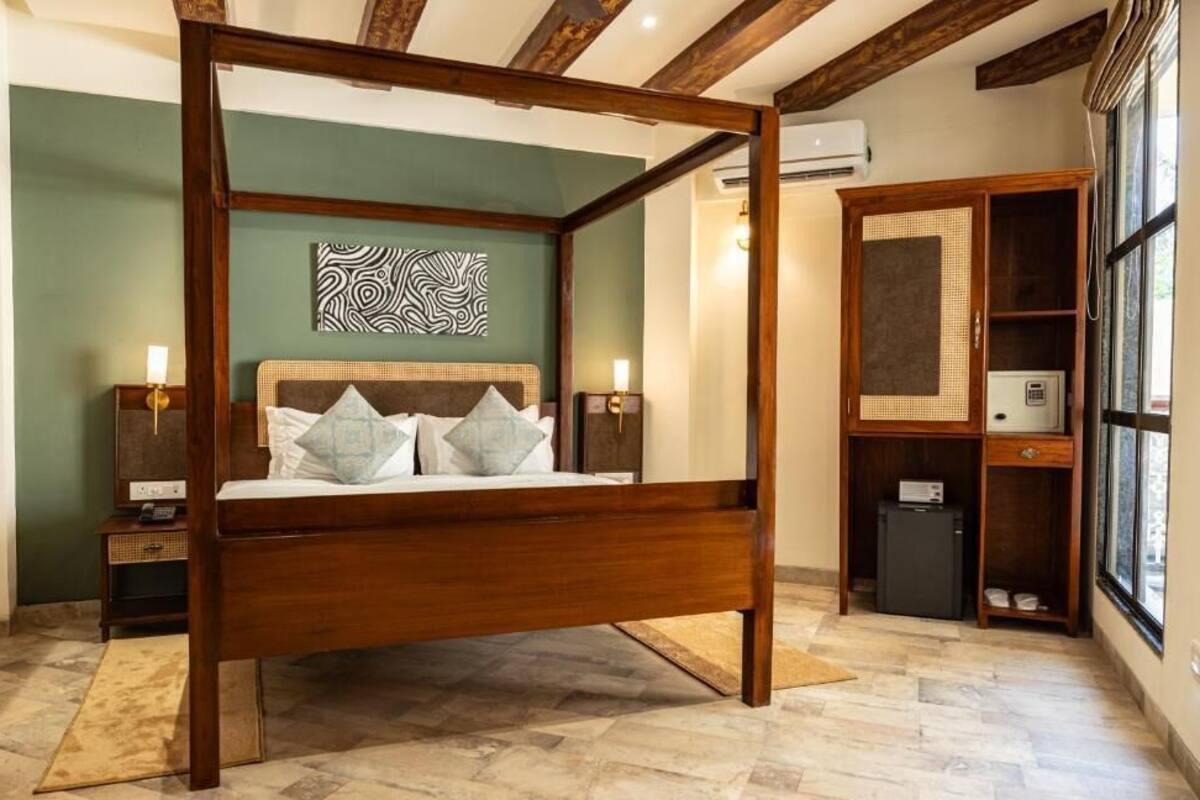 Uma cama com dossel, com cabeceira, mesas de cabeceira, ar condicionado fixado na parede, guarda-roupa embutido e uma janela grande.