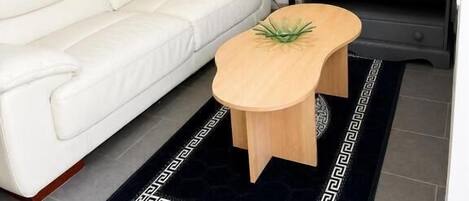 Uma sala de estar com um sofá branco, uma mesa de centro de madeira, um rack preto para TV e um tapete estampado.