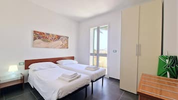 Quarto de hotel com duas camas, uma janela grande, um guarda-roupa e um quadro na parede.