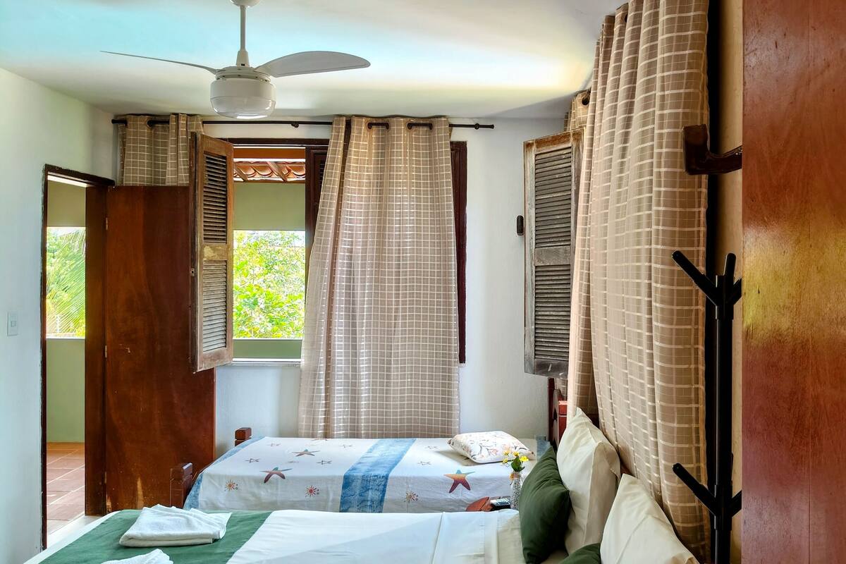 Um quarto com uma cama, um ventilador de teto, uma janela com cortinas e uma placa na parede.