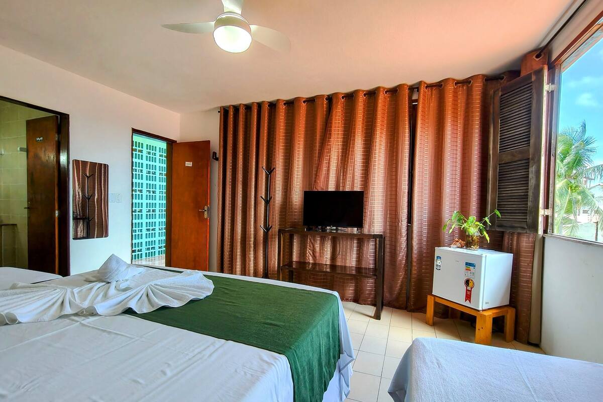 Quarto de hotel com duas camas, televisão, escrivaninha e janela com cortinas.