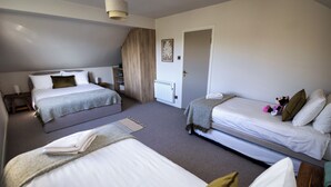 Quarto de hotel com duas camas, um guarda-roupa de madeira, um radiador, uma porta e uma pequena mesa.