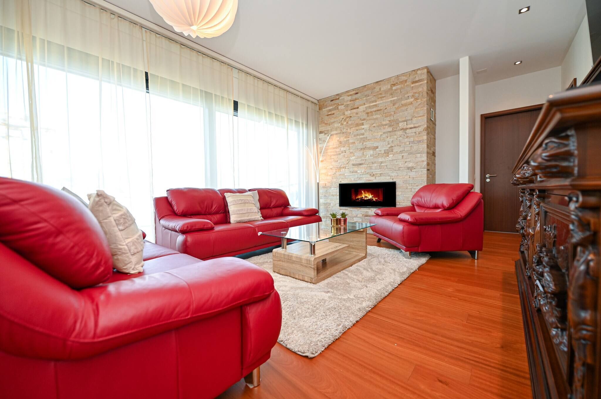 Uma sala de estar moderna com sofás de couro vermelho, uma mesa de centro de vidro, uma lareira e piso de madeira.