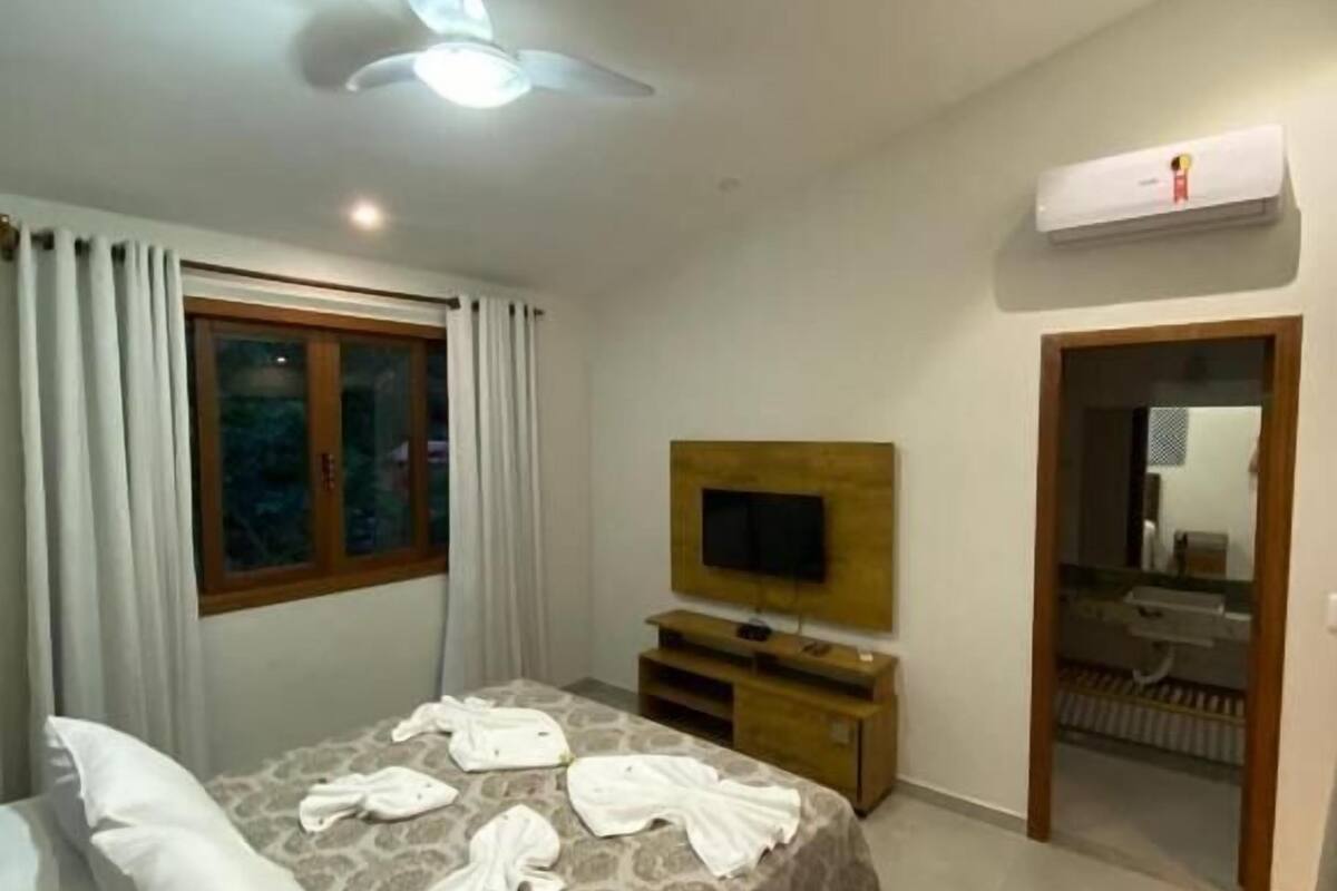 Quarto de hotel com uma cama, televisão, ventoinha no teto e aparelho de ar condicionado.