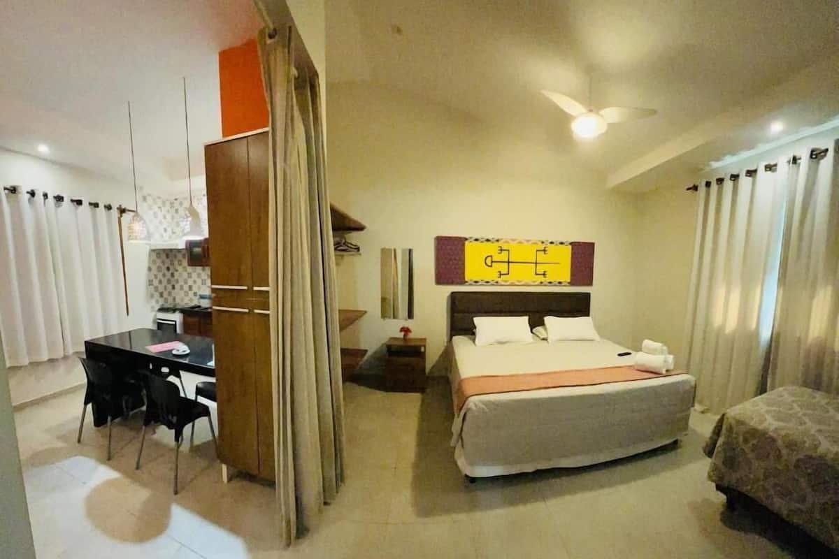 Quarto de hotel com cama, escrivaninha, cadeira, mesa pequena e guarda-roupa.