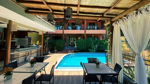 Área de piscina com espaço de estar coberto, bar e vista para um edifício com varandas.