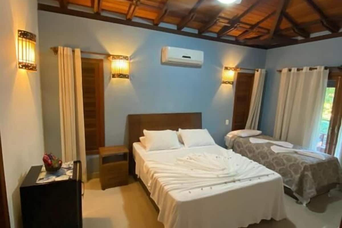 Quarto de hotel com duas camas, ventoinha no teto, ar condicionado na parede e abajures.