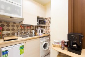 Uma kitchenette compacta com micro-ondas, torradeira, máquina de lavar e cafeteira.