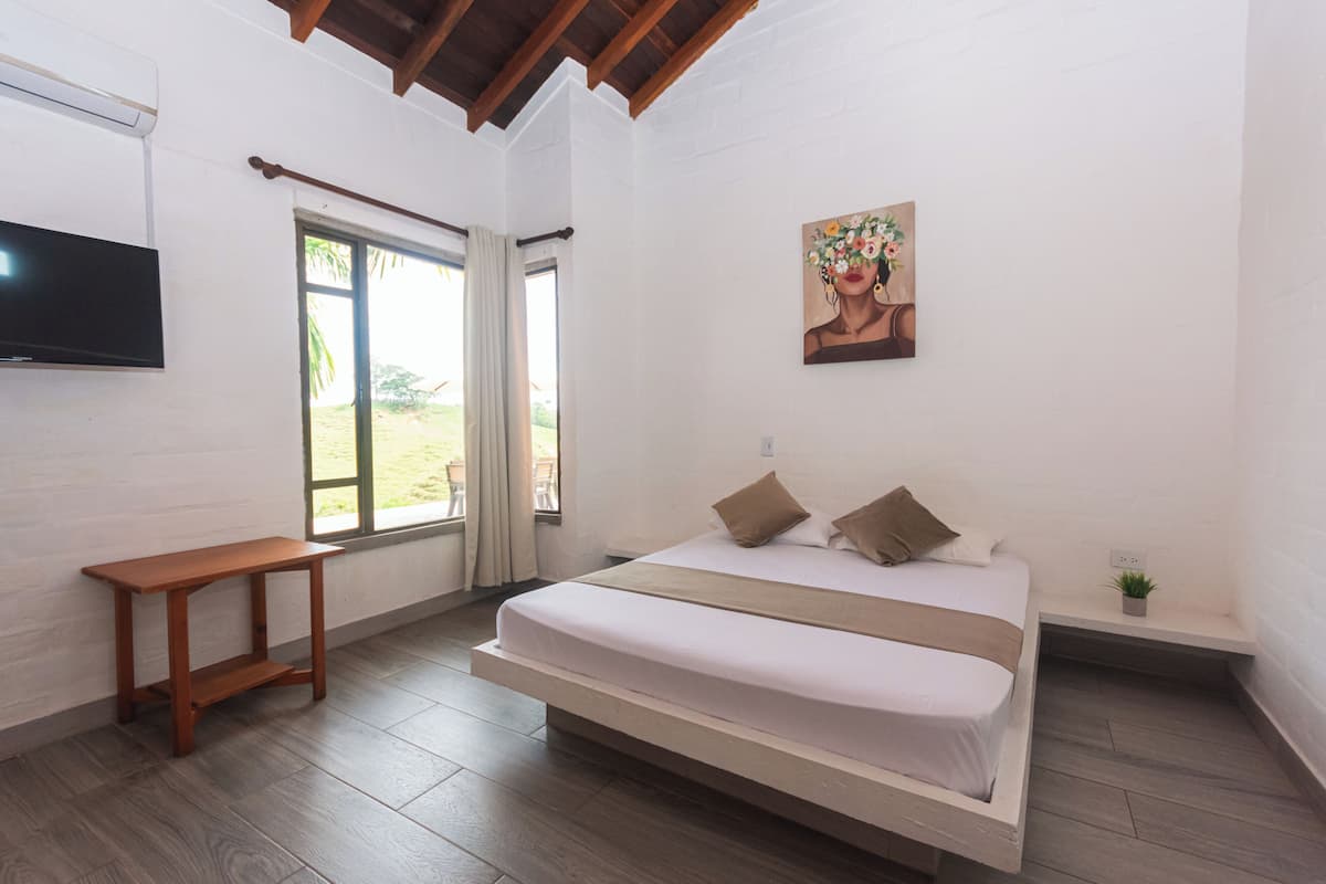Um quarto com uma cama, uma televisão, uma janela e um quadro na parede.