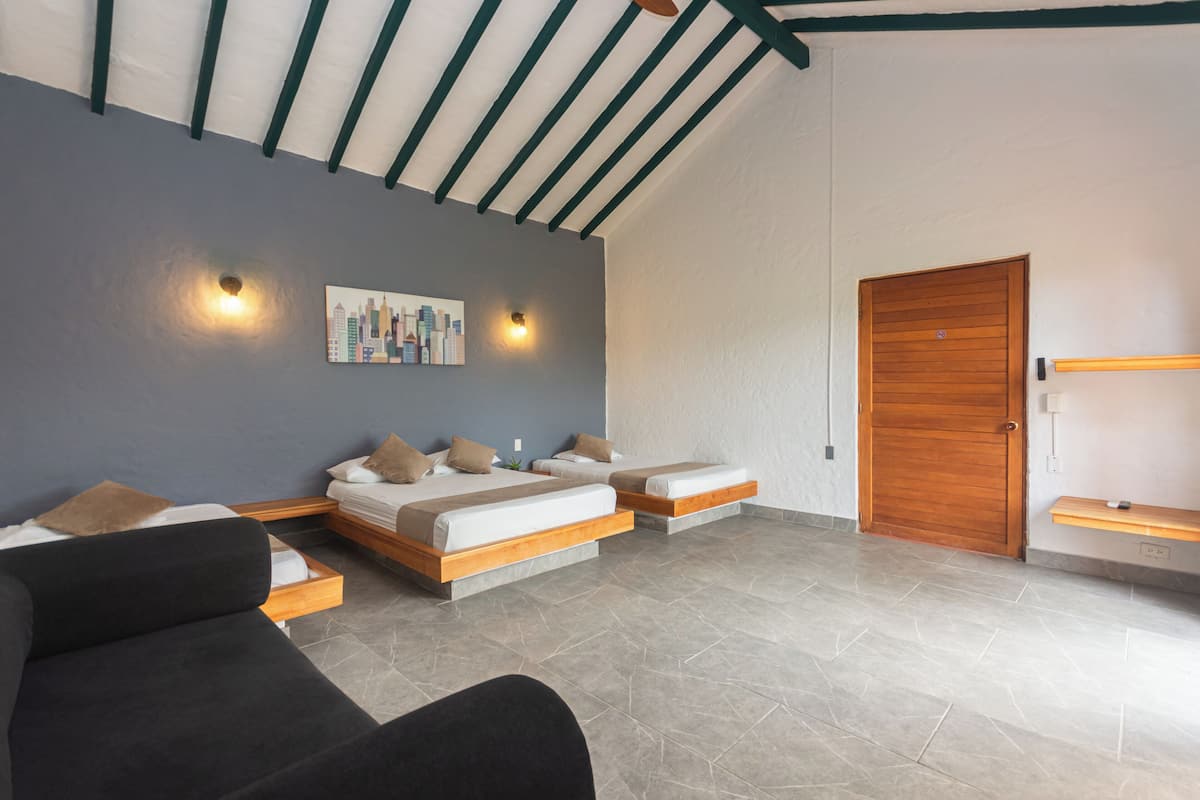 Quarto moderno com duas camas, um sofá, uma porta de madeira e uma pintura de paisagem urbana.
