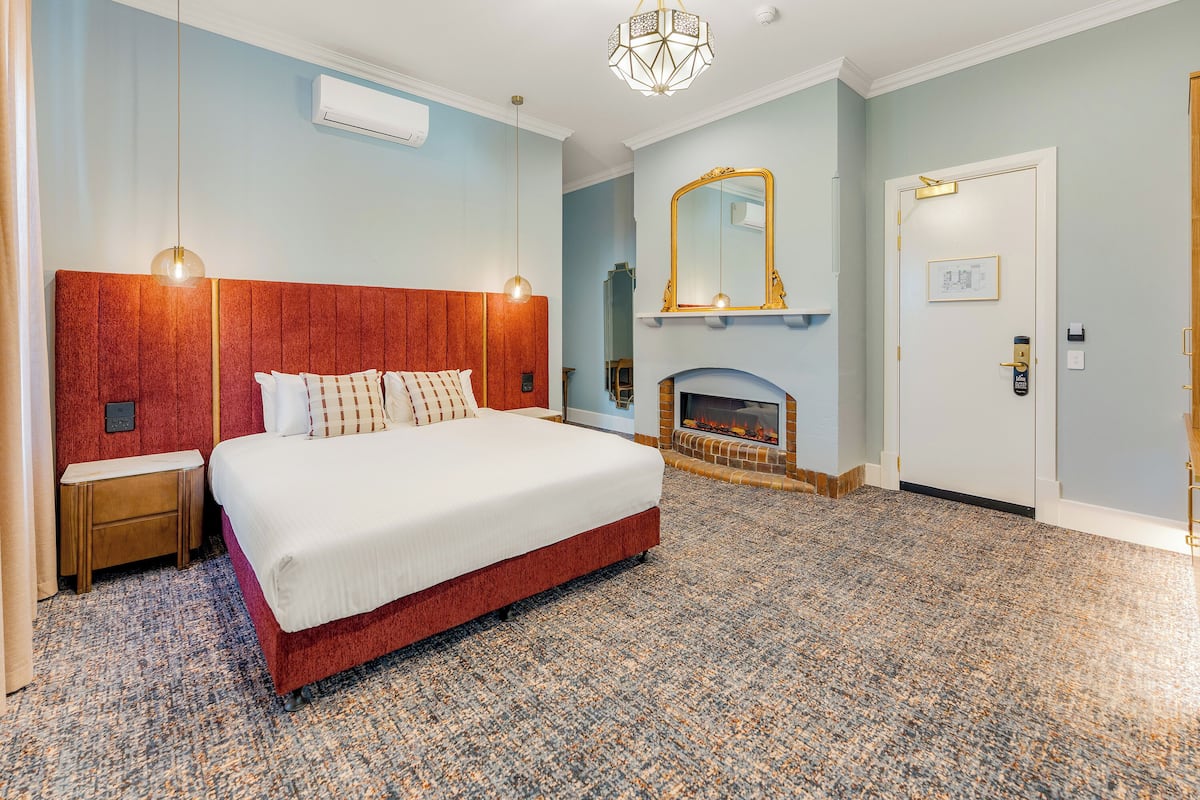 Quarto de hotel com uma cama grande, lareira, espelho e porta com fechadura.