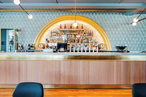 Uma área de bar com balcão de madeira, parede estampada e um amplo mostrador em arco com garrafas.