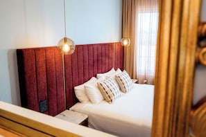 Uma cama com cabeceira vermelha, roupa de cama branca e duas luminárias de apoio.
