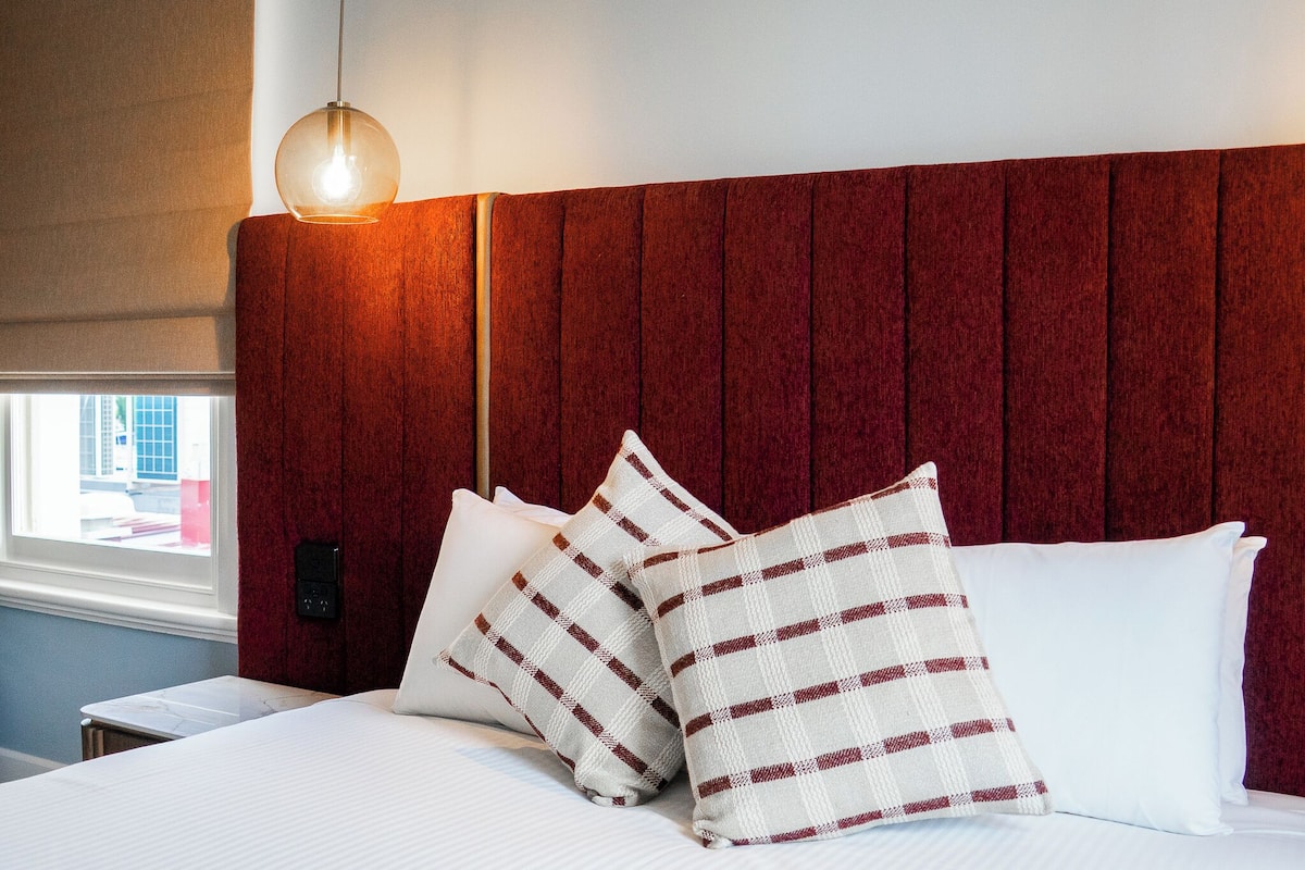 Uma cama com roupa de cama branca, cabeceira vermelha e almofadas listradas.