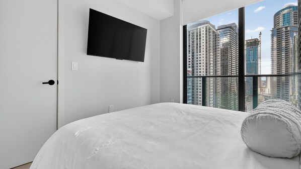 Quarto com cama, televisão de tela plana na parede e grande janela com vista para a cidade.