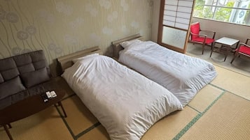 Quarto com duas camas, um sofá, uma mesinha e vista para o verde pela janela.