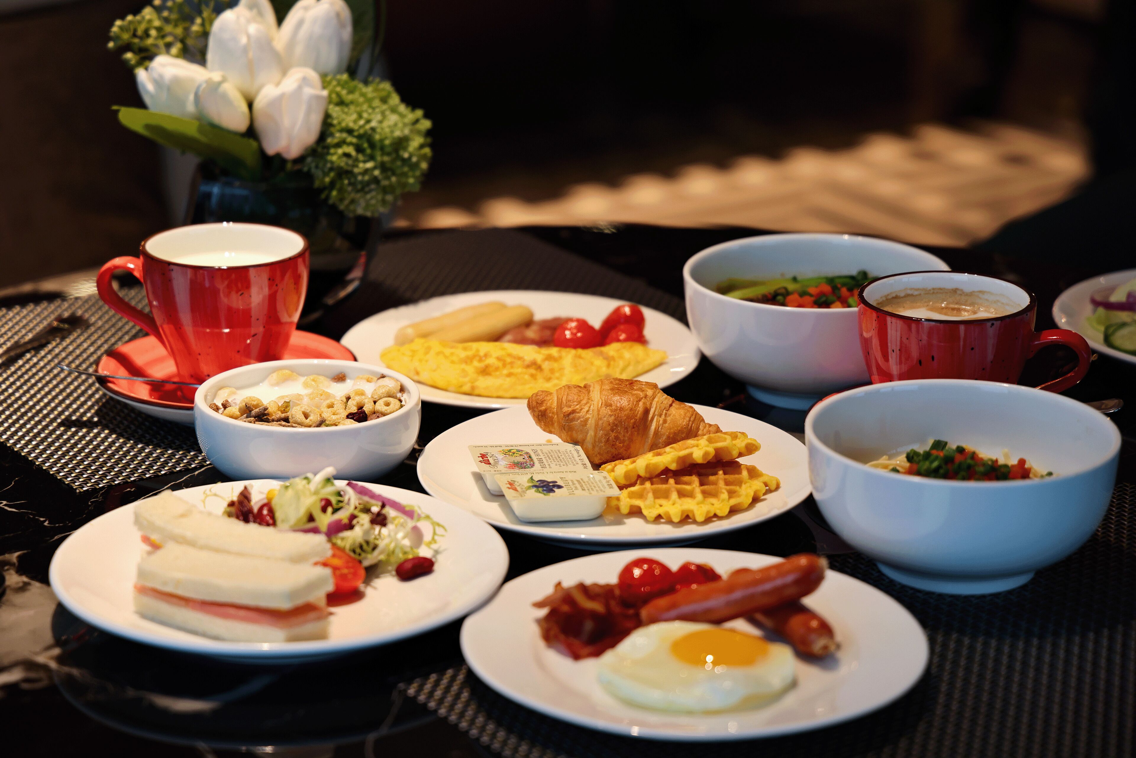 Uma mesa posta com diversos itens de café da manhã, incluindo ovos, torradas, waffles e um croissant.