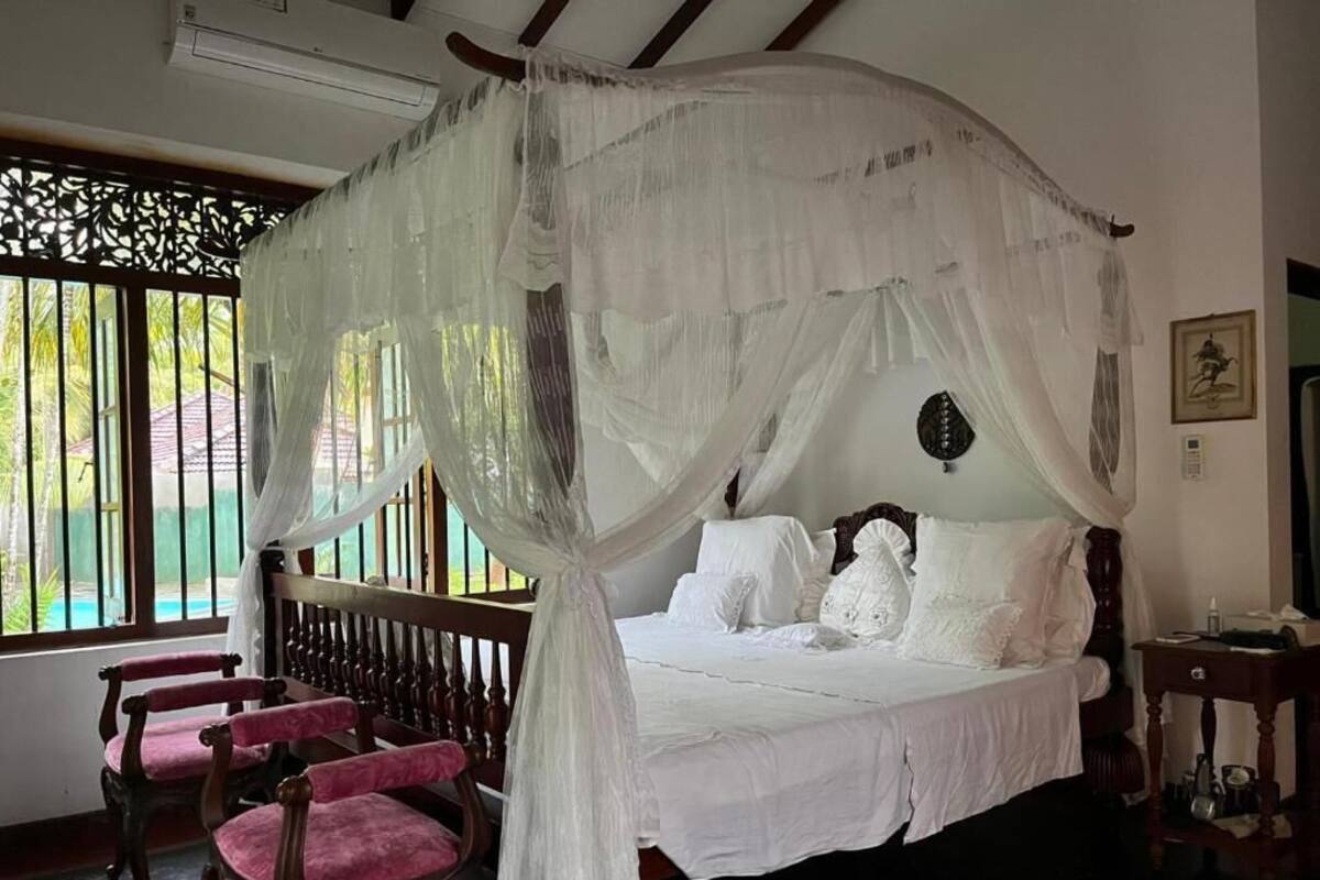 Quarto com uma cama de dossel, uma cadeira de madeira e janela com vista para o verde.