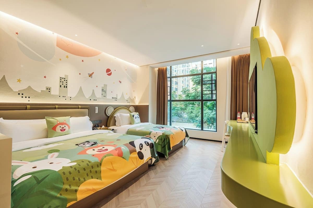 Quarto de hotel com duas camas, uma janela grande, um espelho e uma parede com design de paisagem urbana.