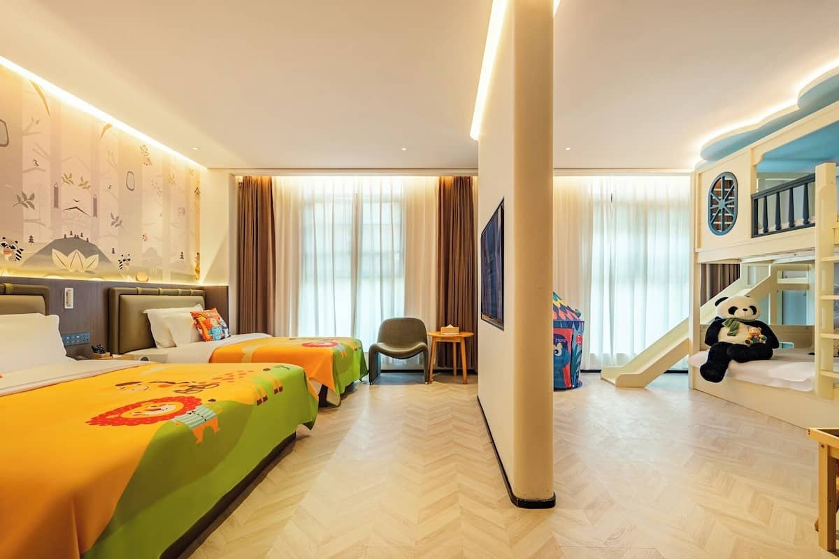 Quarto de hotel com duas camas, uma escrivaninha, uma cadeira, uma televisão, um sofá e uma beliche.