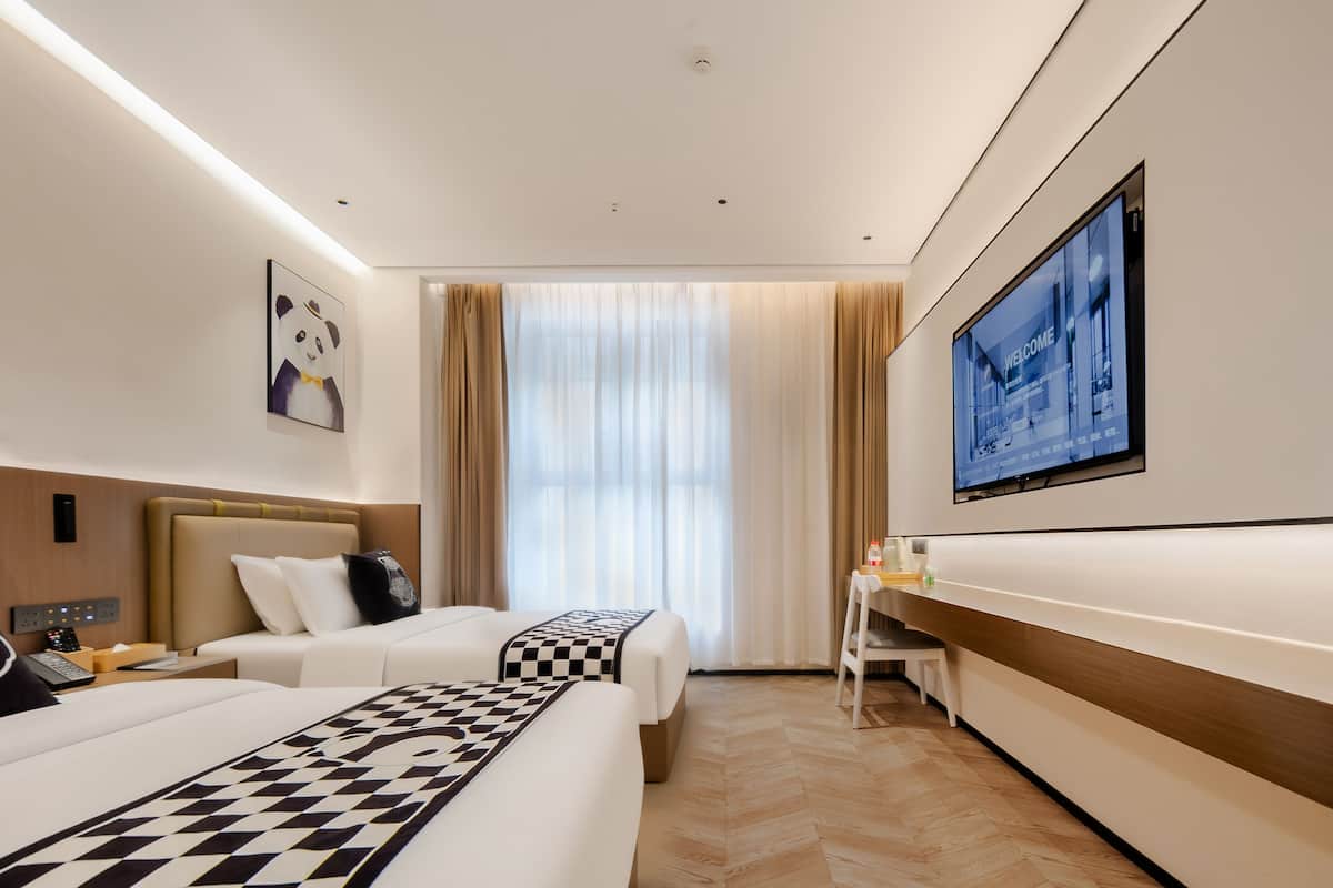 Quarto de hotel com duas camas, uma escrivaninha, televisão e uma janela grande com cortinas.