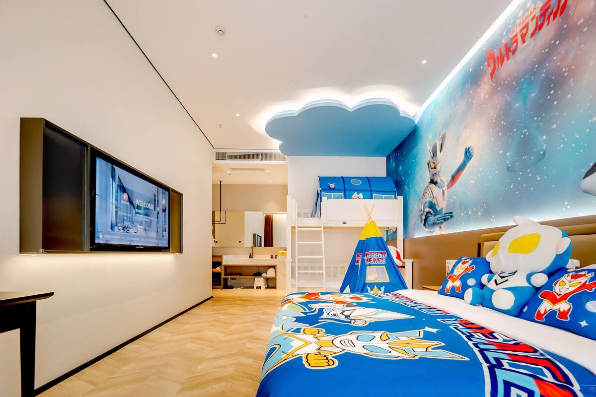 Quarto de hotel moderno com cama grande, televisão, beliche e parede com um mural com tema espacial.