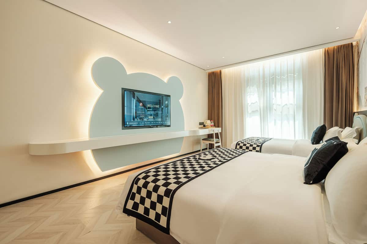 Quarto de hotel com cama grande, televisão fixada na parede, escrivaninha e janela com cortinas.