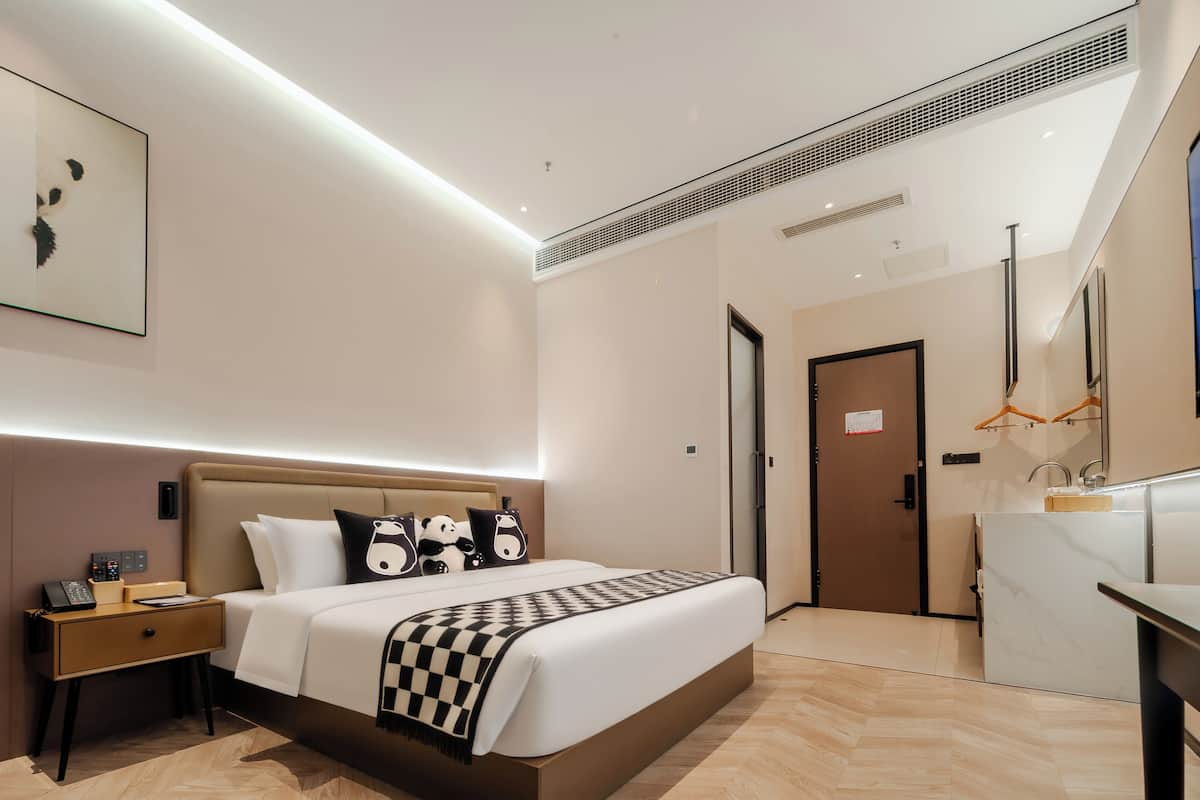 Quarto de hotel moderno com uma cama grande, mesa de cabeceira e escrivaninha com cadeira.