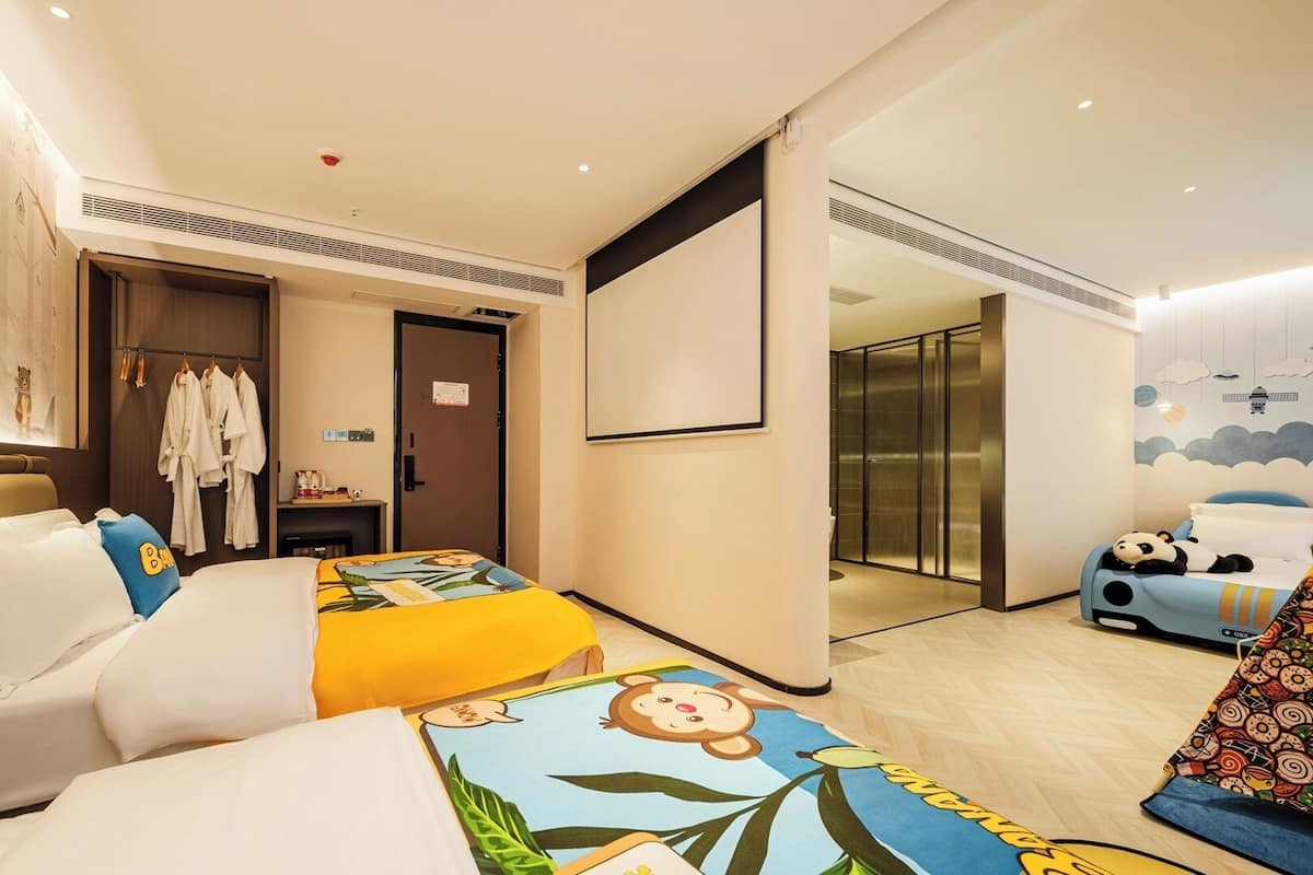 Quarto de hotel com duas camas, um sofá, um guarda-roupa, um espelho e uma parede com um mural de nuvens.