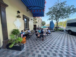 Uma área externa com mesas e cadeiras, um toldo azul e piso xadrez.
