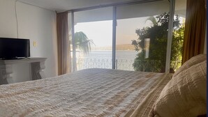 Quarto de hotel com uma cama grande, uma televisão em suporte e vista para o mar através de amplas janelas.