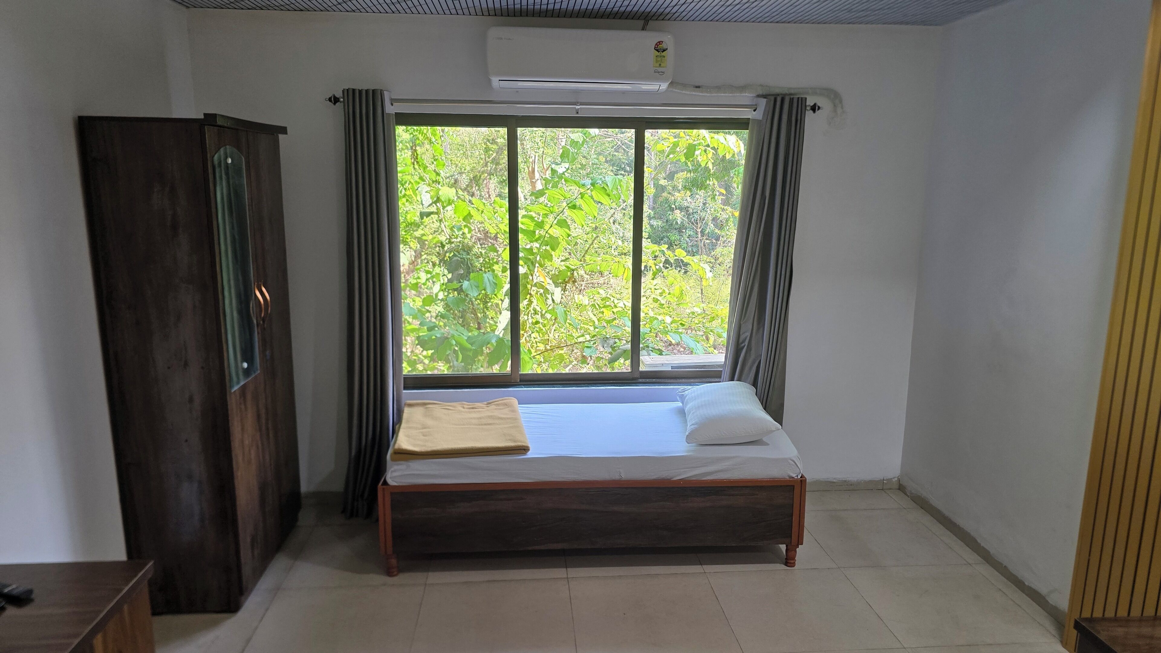 Quarto com cama, guarda-roupa, janela com cortinas e ar condicionado.