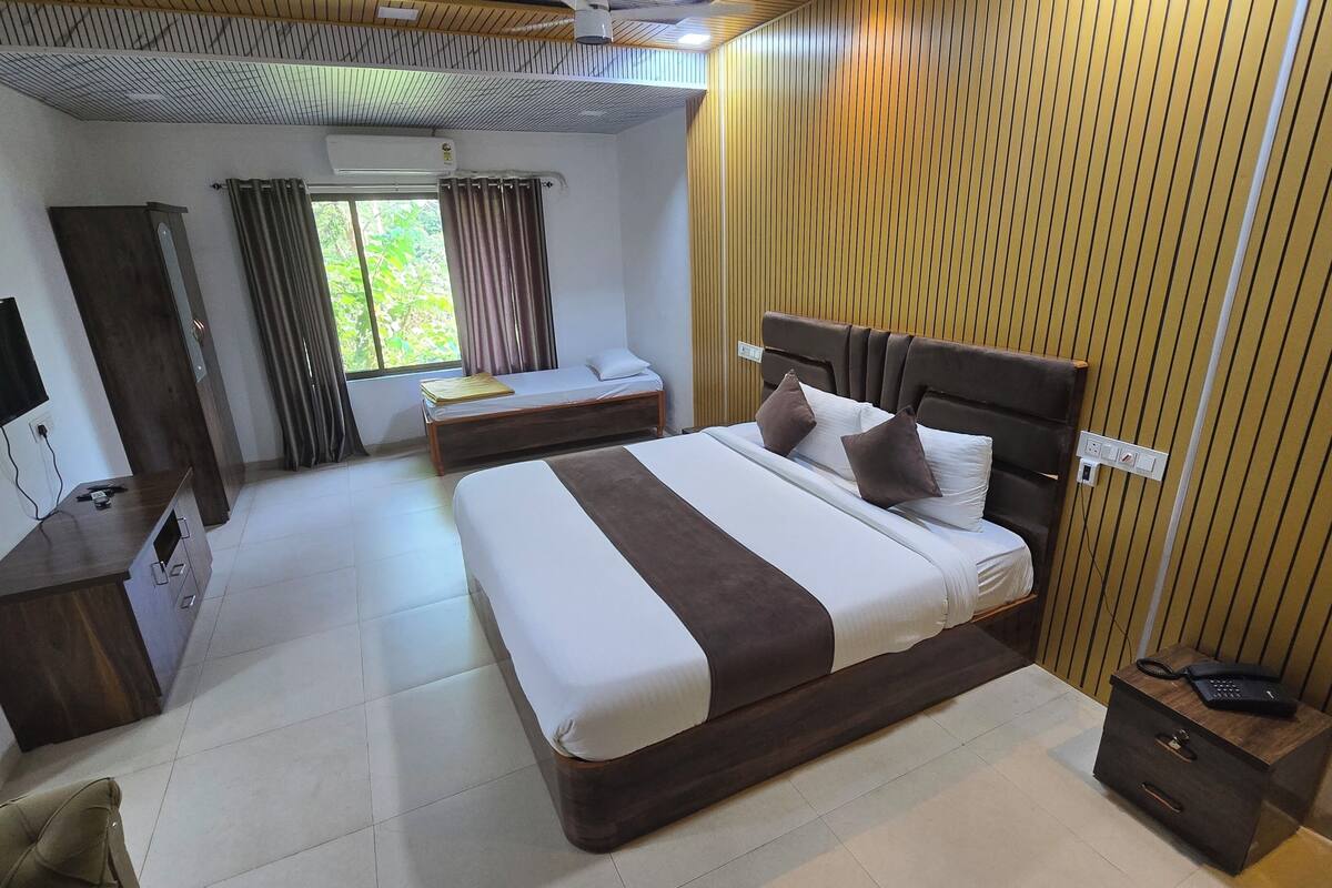 Quarto de hotel com uma cama grande, uma escrivaninha, uma televisão e uma janela com cortinas.