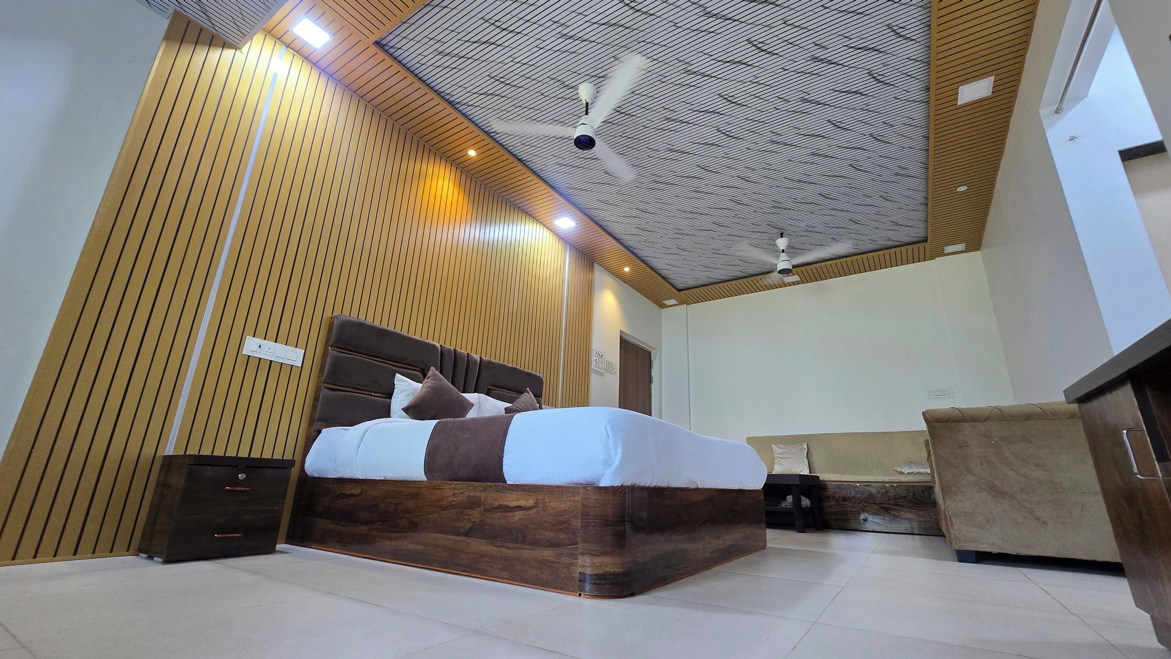 Quarto moderno com cabeceira de madeira, cama com roupa de cama branca e marrom, ventilador de teto e parede de destaque em madeira.